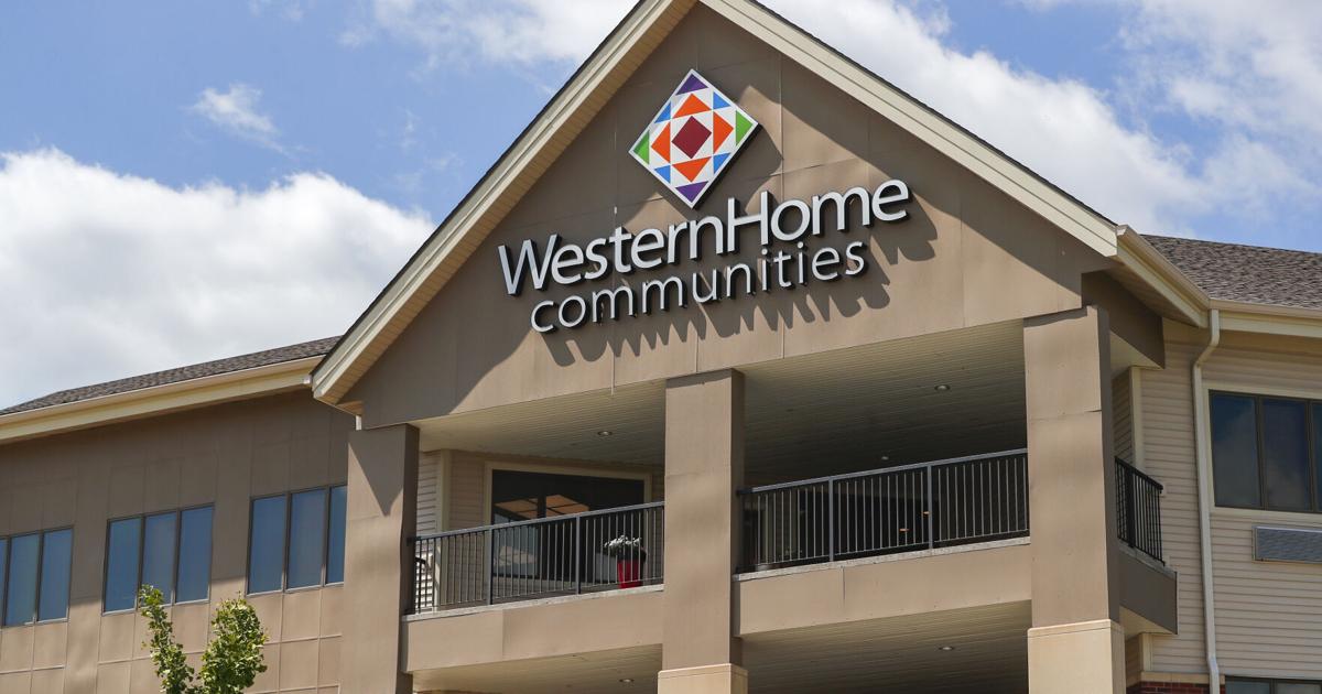 A long-term health facility exterior on a blue sunny day with their logo on the front.